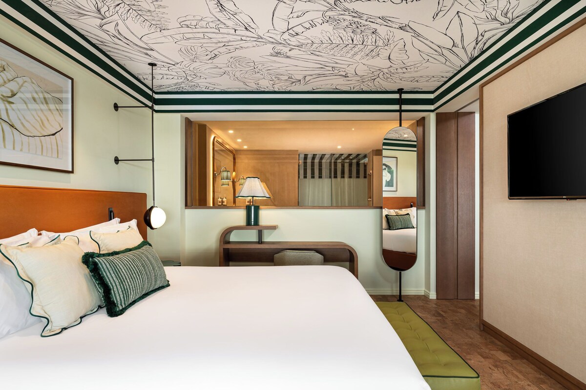 Quarto de hotel com uma cama grande, escrivaninha, espelho e televisão de tela plana.