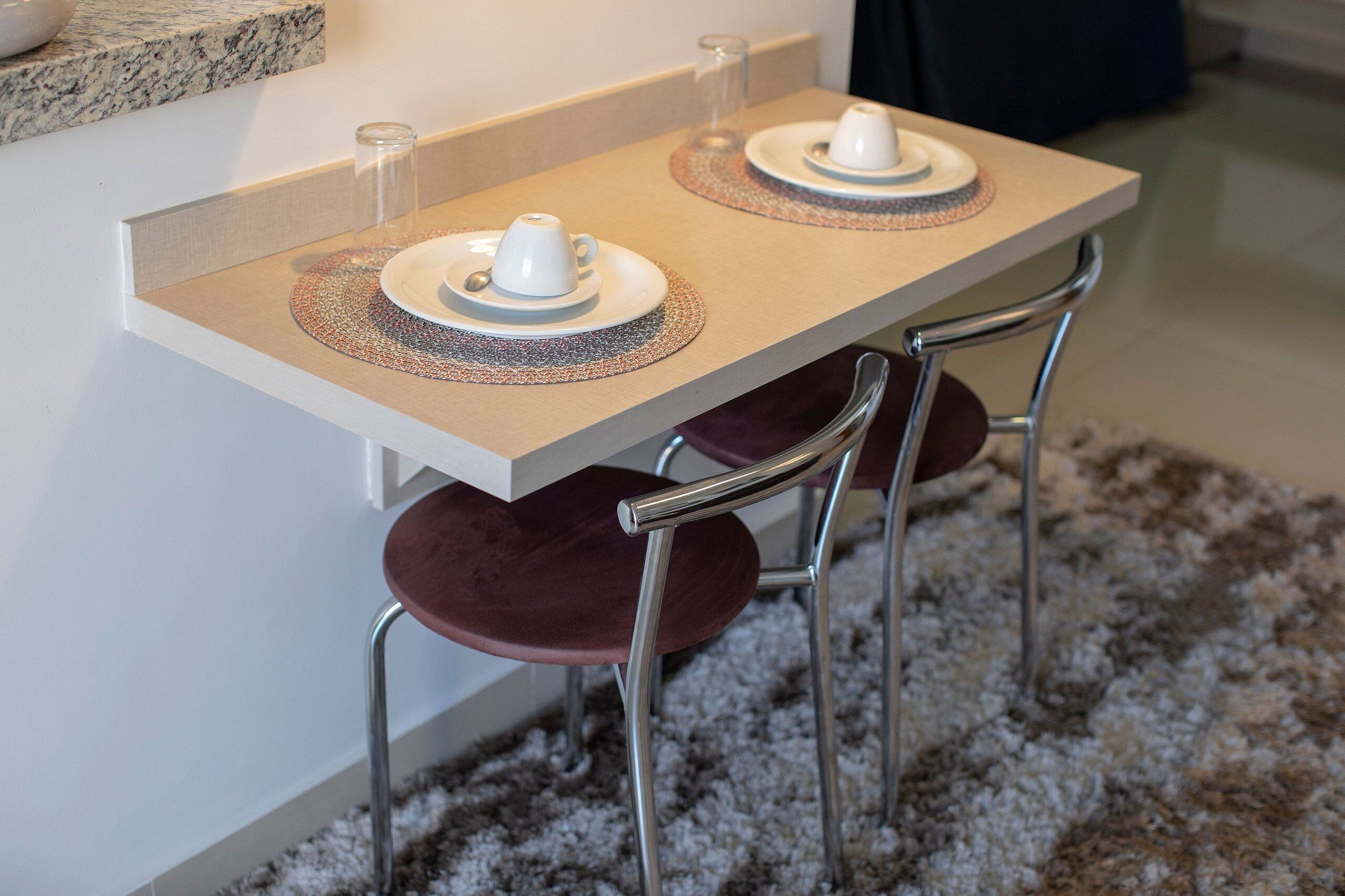 A small table with two white cups on saucers, a spoon, and a woven placemat.
