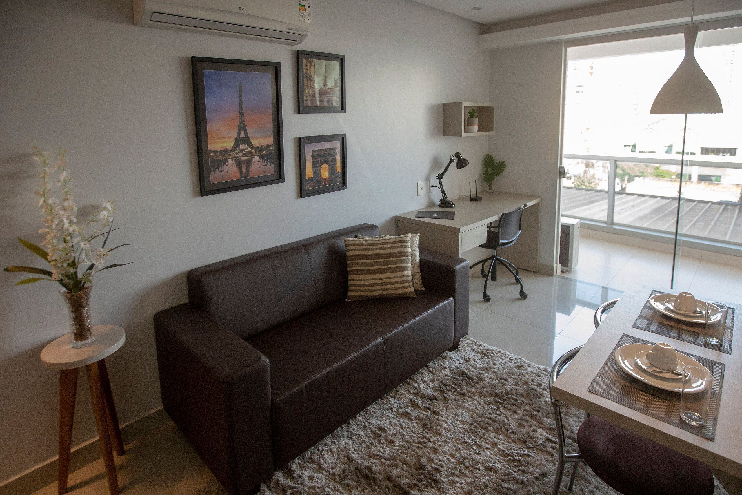 Uma sala de estar moderna com um sofá, uma mesa de jantar posta para dois e quadros nas paredes.