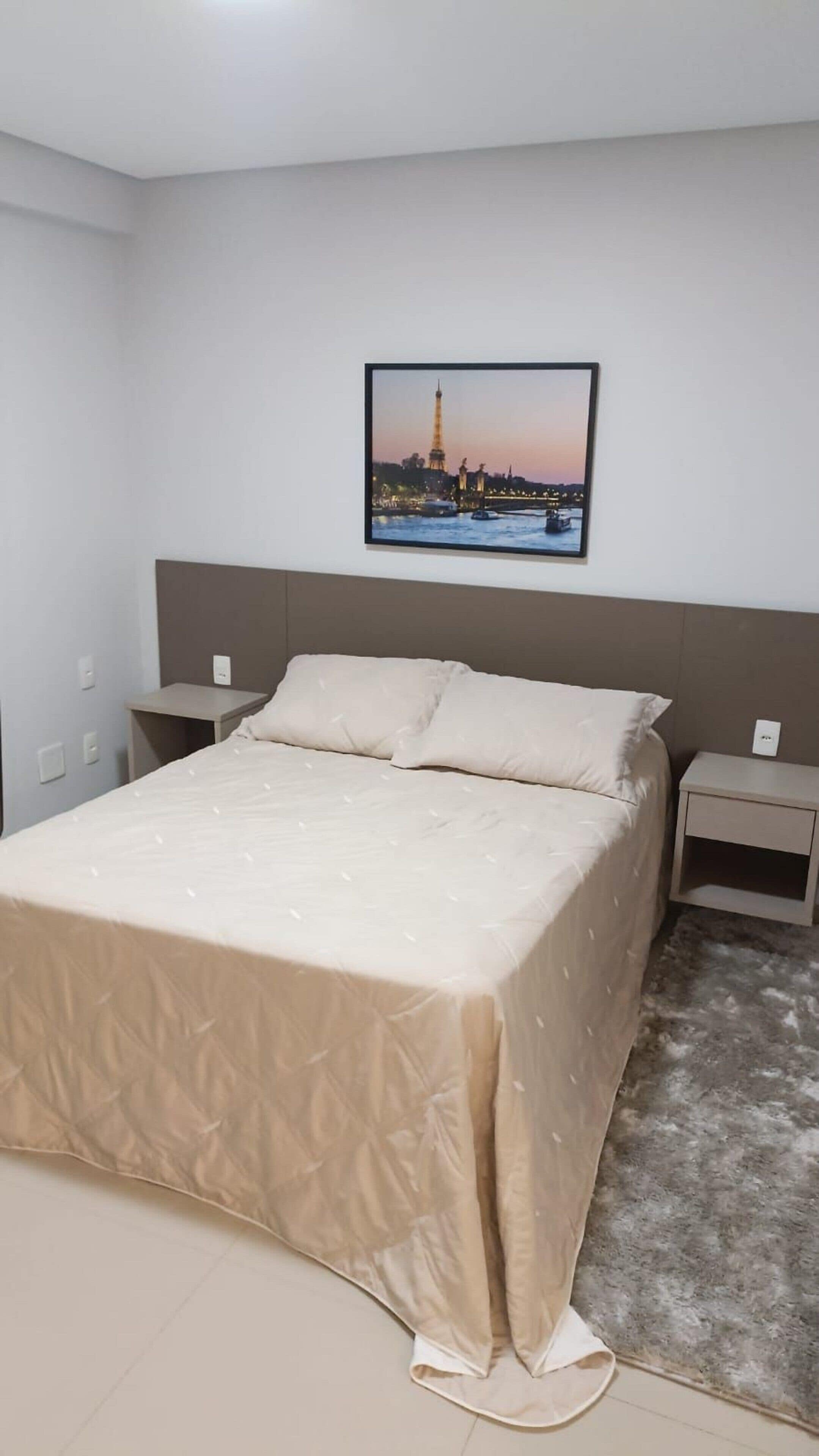 Quarto com uma cama, duas mesas de cabeceira e uma imagem da Torre Eiffel na parede.