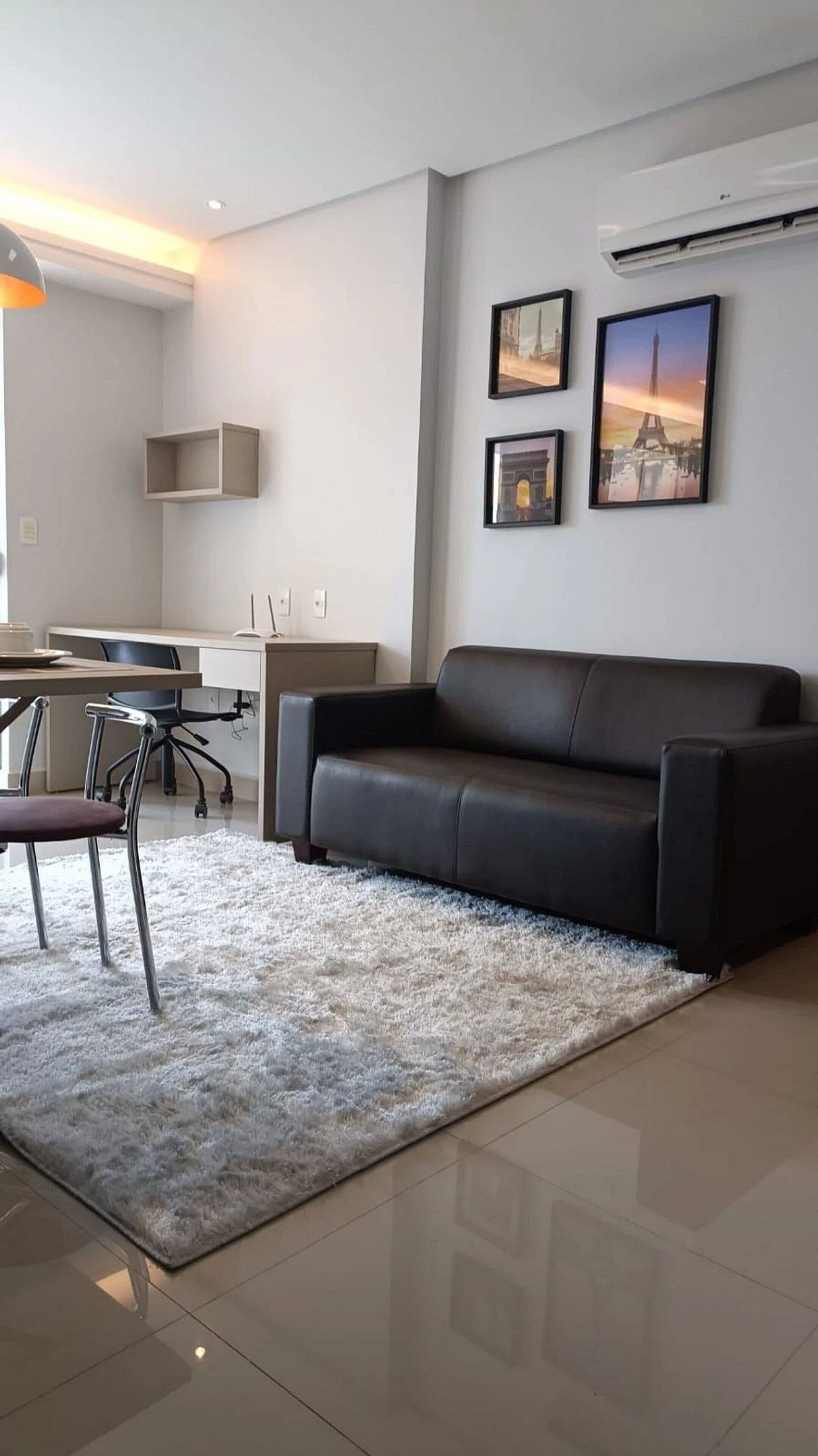Uma sala de estar moderna com um sofá de couro preto, um tapete felpudo branco e uma escrivaninha com cadeira.