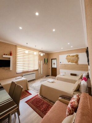 Quarto de hotel com duas camas, uma mesa de jantar, televisão e janela com persianas.