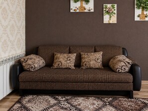 Um sofá marrom com almofadas estampadas, um tapete padronizado e uma parede com três obras de arte emolduradas.