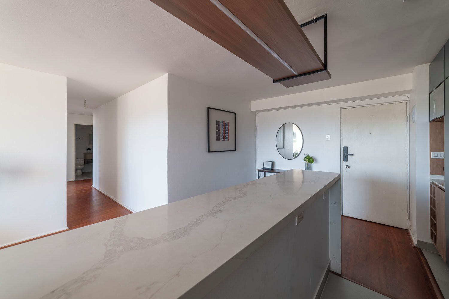 Uma cozinha moderna com bancada de mármore, viga de madeira no teto, um quadro na parede e uma porta que dá para outro cômodo.