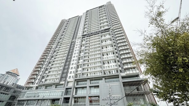 Um edifício alto com várias varandas, um espaço comercial no andar térreo e sinalização para 'YOSHINOYA JAPAN'S No.1 Beef Bowl'.