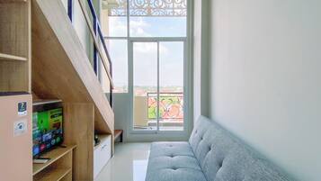 Quarto com sofá cinza, estantes de madeira, escada e uma janela grande com vista para edifícios.
