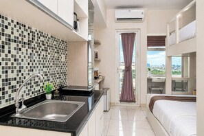 Quarto de hotel compacto com cozinha compacta, uma cama, janela com cortina e aparelho de ar condicionado.