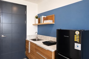 Cozinha com geladeira preta, pia, armários de madeira, bancada de mármore e parede azul.