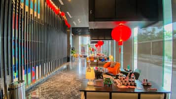 Um lobby de hotel moderno com um corredor longo, painéis verticais coloridos e uma área de estar com uma mesa exibindo maquetes de casas.