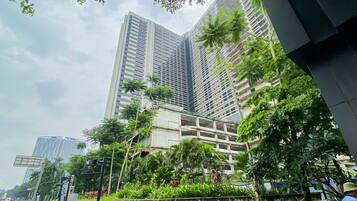 Um moderno edifício alto com fachada mista de vidro e concreto, rodeado por vegetação exuberante e palmeiras.