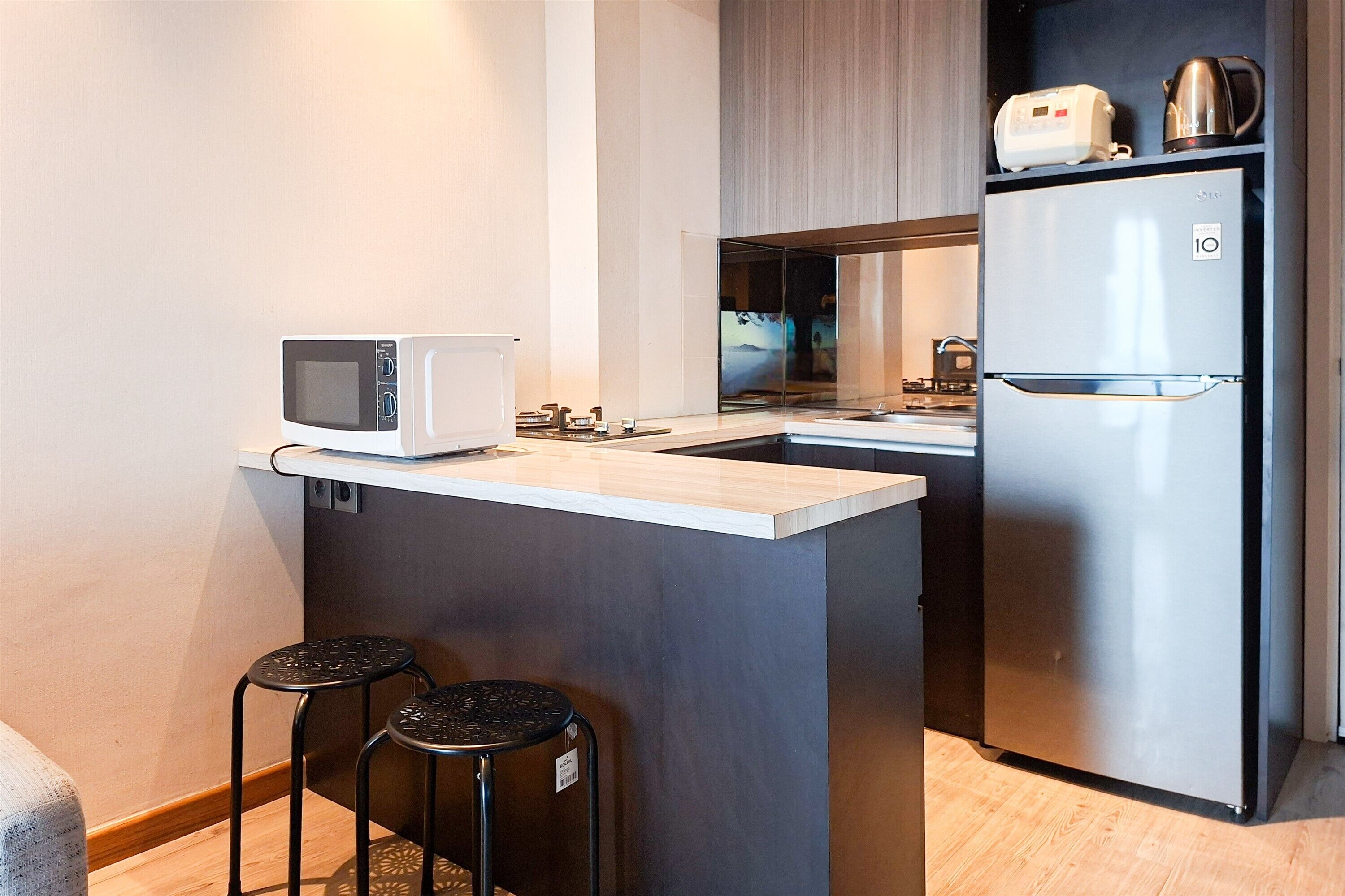 Cozinha compacta com micro-ondas, geladeira de aço inoxidável e dois bancos.