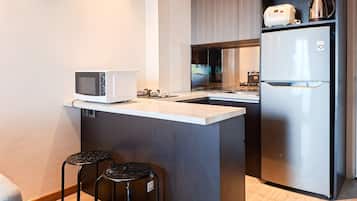 Cozinha compacta com micro-ondas, geladeira de aço inoxidável e dois bancos.
