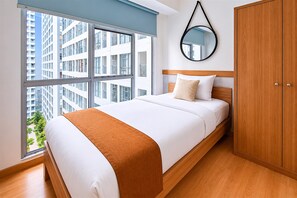 Quarto de hotel moderno com uma janela grande, cama, guarda-roupa e espelho.