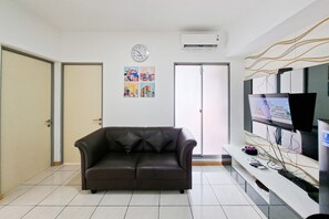 Quarto com sofá de couro preto, um relógio, ar condicionado na parede e uma televisão.