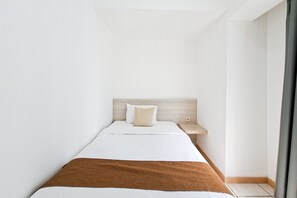 Uma cama de solteiro com cabeceira de madeira, uma mesinha de cabeceira e um manta marrom.