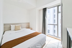 Quarto de hotel com uma cama grande, cabeceira de madeira, mesa de cabeceira e vista para um prédio pela janela.