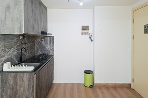 Uma cozinha com pia, fogão e armários, uma lixeira e uma porta com telefone e interruptor de luz.