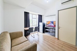 Uma sala de estar com um sofá, uma televisão, uma escrivaninha com cadeiras e uma porta.