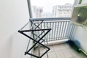 Uma varanda com um varal de metal, uma janela com vista para edifícios altos e um aparelho de ar condicionado.