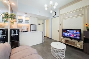 Cozinha moderna com eletrodomésticos embutidos, sala de jantar com mesa e cadeiras brancas e uma TV de tela plana em um suporte de madeira.