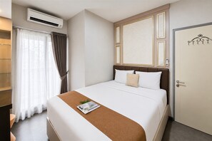 Quarto de hotel com cama, janela com cortinas, ar condicionado, porta com maçaneta e interruptor de luz fixado na parede.