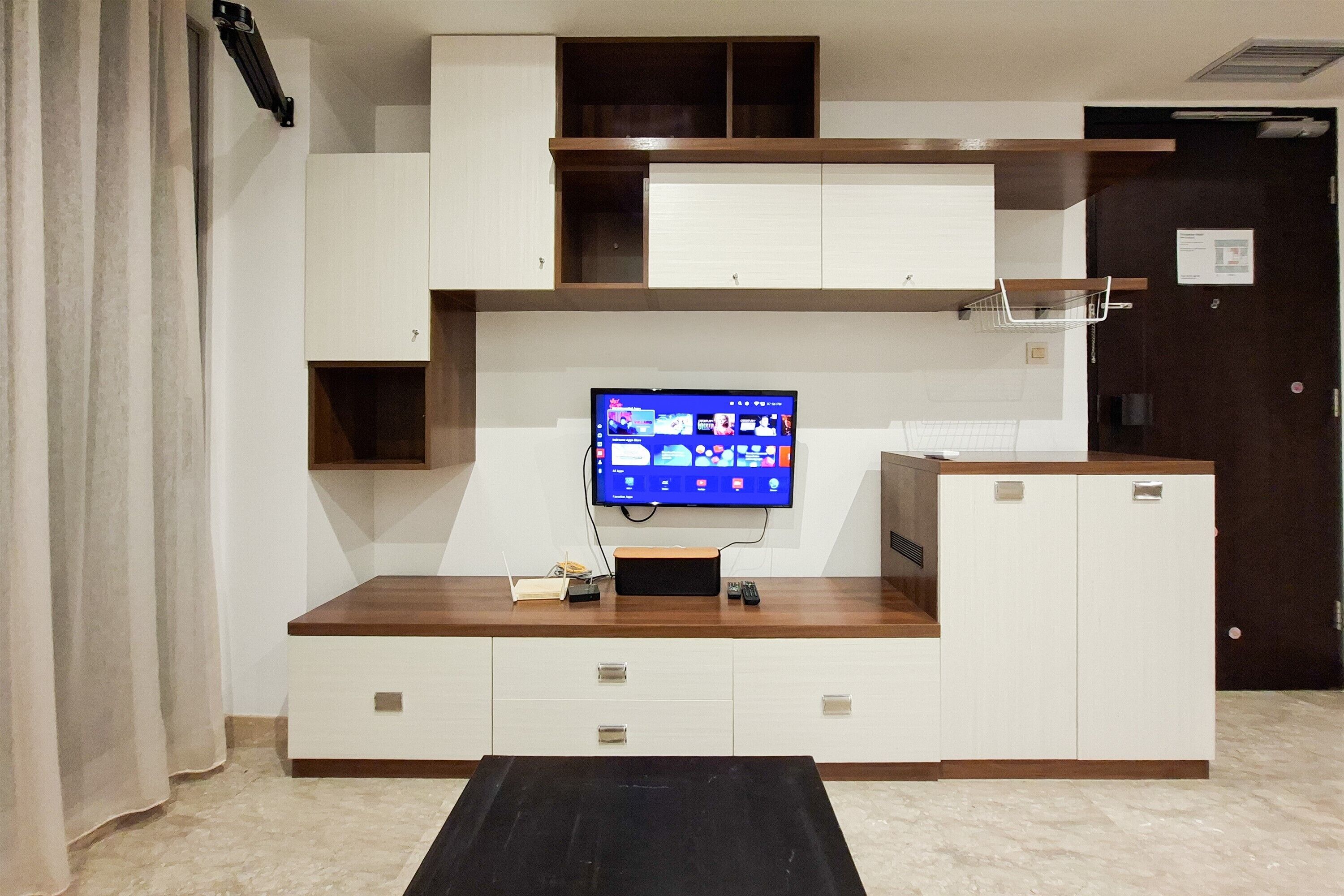 Quarto com televisão de tela plana presa a um armário branco, uma escrivaninha de madeira com gavetas e piso escuro.
