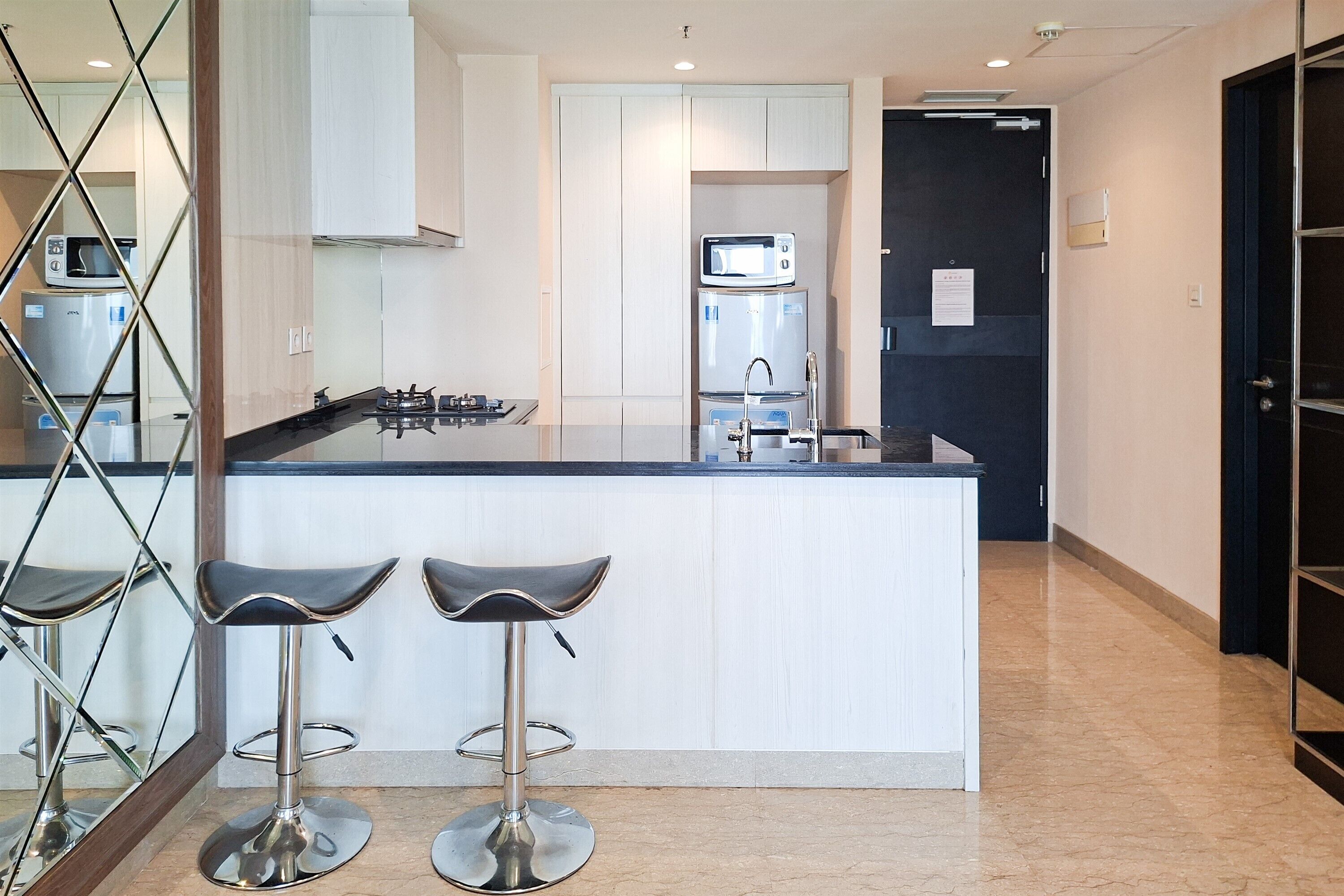 Uma cozinha moderna com uma ilha central, três banquetas altas, eletrodomésticos de aço inoxidável e uma porta escura.
