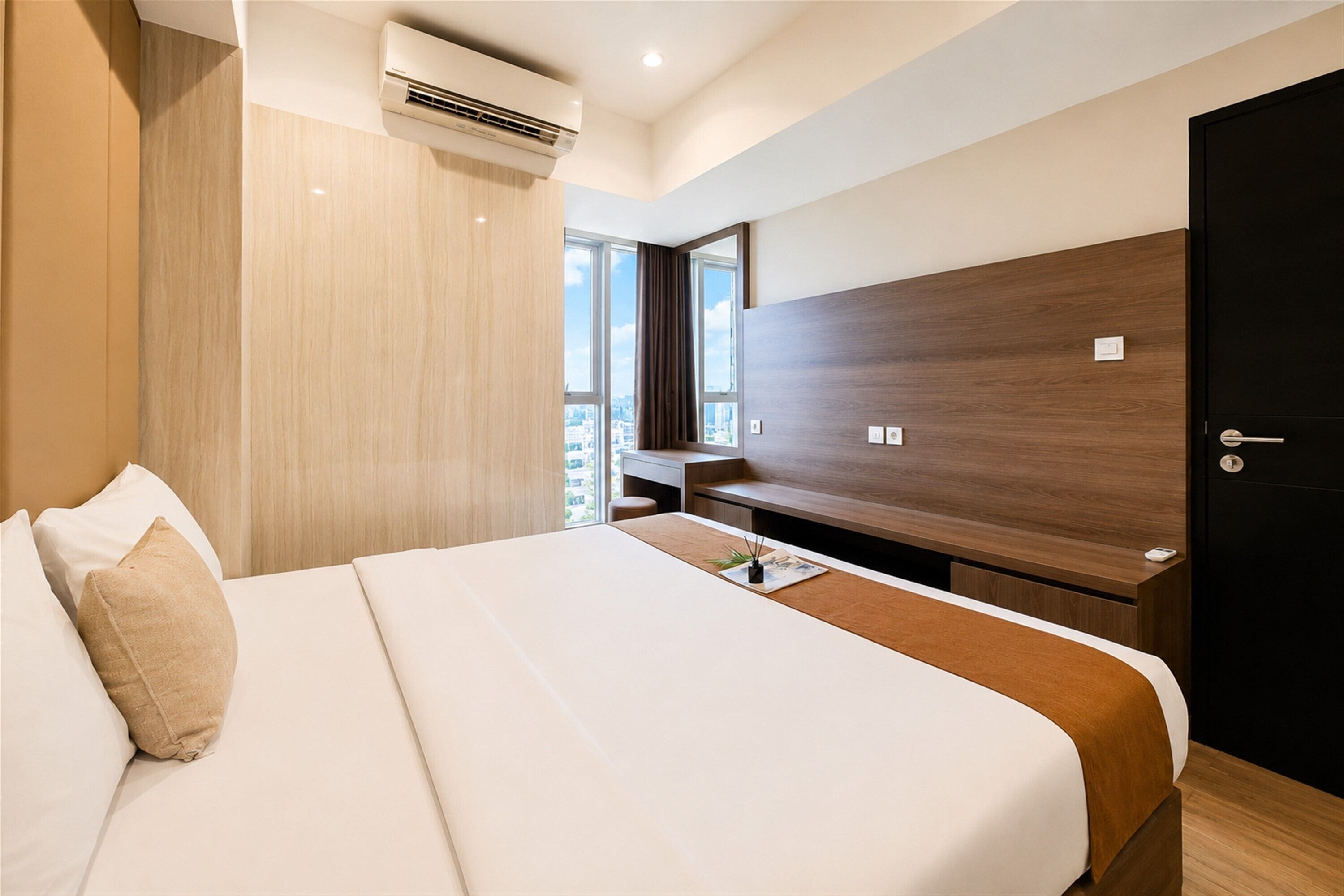 Quarto de hotel moderno com uma cama grande, cabeceira de madeira, escrivaninha e guarda-roupa.