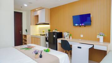 Quarto de hotel com uma cama, uma escrivaninha, uma televisão, um mini-frigobar, micro-ondas e uma pequena cozinha.