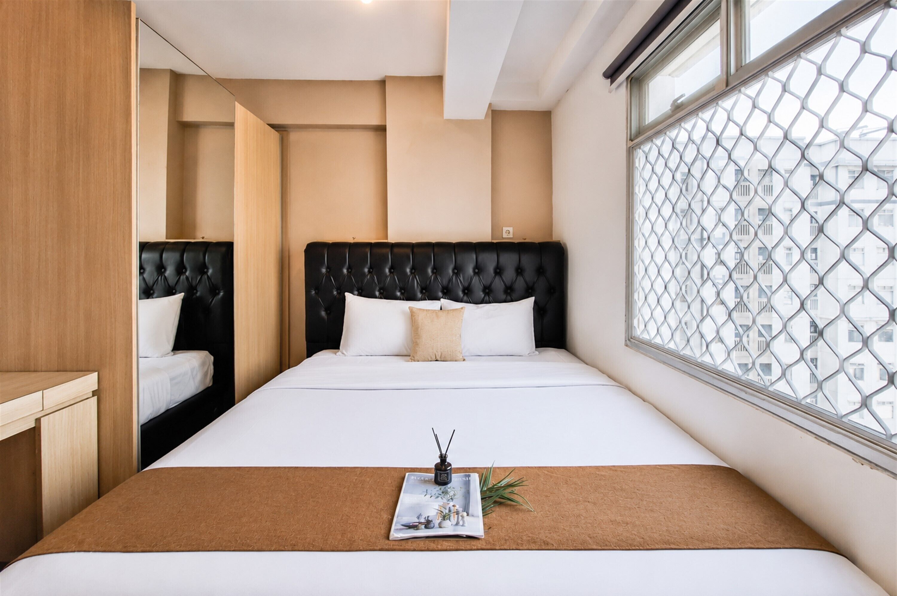 Quarto de hotel com uma cama grande, uma janela com grade de metal e cabeceira de madeira.
