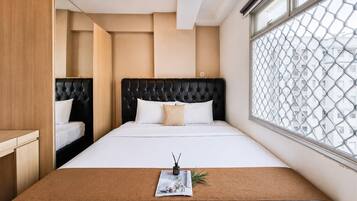 Quarto de hotel com uma cama grande, uma janela com grade de metal e cabeceira de madeira.