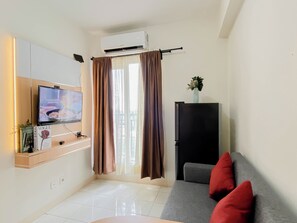 Uma sala de estar moderna com televisão de tela plana, um sofá com almofadas vermelhas, um armário preto e uma janela com cortinas.