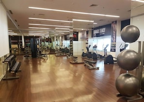 Uma academia com diversos equipamentos de exercício, incluindo esteiras, bicicletas ergométricas e pesos livres.