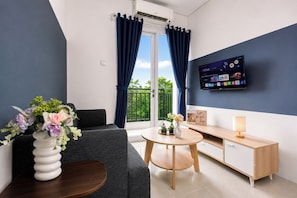 Uma sala de estar moderna com sofá, mesa redonda, TV fixada na parede e varanda com cortinas.