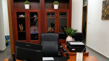 Uma mesa de recepção com um monitor Planar, uma cadeira de escritório preta, um armário de madeira com portas de vidro e uma placa com a inscrição 'HOSTAL SANTA BARBARA'.