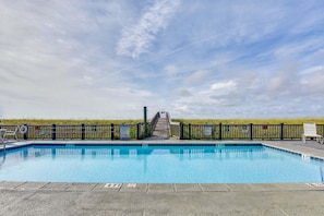 Uma piscina com deck de madeira, um posto de salva-vidas e vista para a praia.