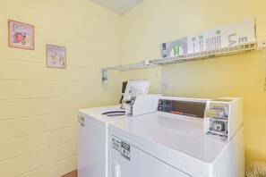 Uma área de lavanderia com máquina de lavar frontal, secadora e uma prateleira acima da secadora com uma placa.