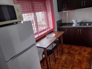 Uma cozinha compacta com geladeira, micro-ondas, pia e uma mesa de madeira.