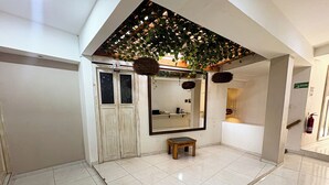 Um quarto com um espelho grande, um banquinho pequeno, uma porta com uma placa e um teto com padrão trançado.