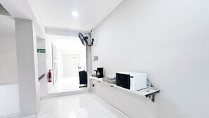 Um corredor com chão de azulejos brancos, um ventilador de teto, micro-ondas e máquina de café em uma prateleira.
