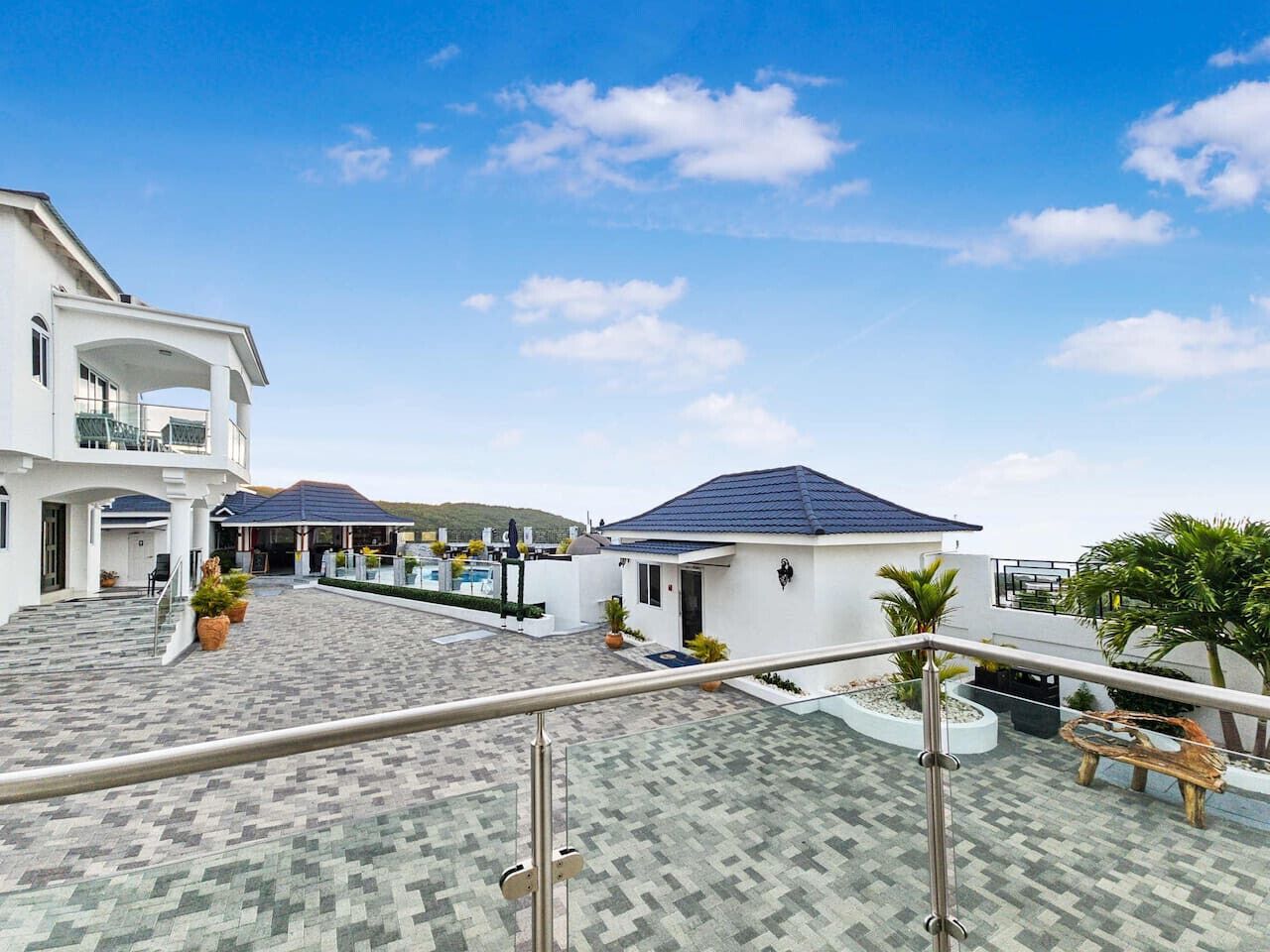 Um hotel moderno com área externa ampla, piso de azulejos estampados, piscina e um pequeno edifício com telhado azul.