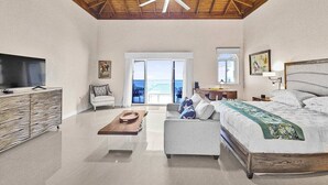 Quarto espaçoso com uma cama grande, ventilador de teto, televisão e vista para o mar através das portas da varanda.