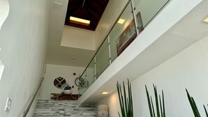 Uma escadaria moderna com guarda-corpos de vidro, parede de pedra e uma grande planta.