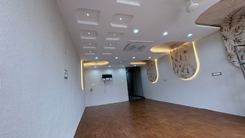 Interior de um hotel moderno com piso de madeira, iluminação embutida e painéis decorativos na parede.