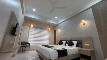 Quarto moderno com cama, mesa de cabeceira, cadeira, ventilador de teto e televisão fixada na parede.