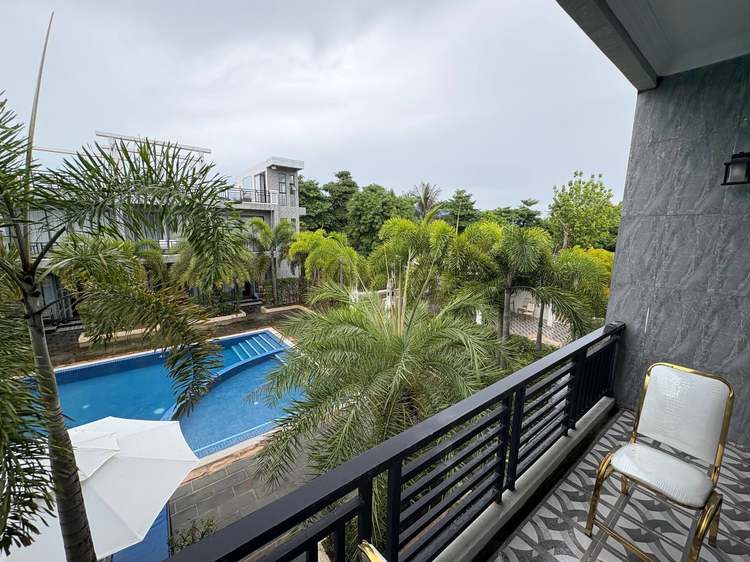 Uma varanda com vista para uma piscina, cercada por vegetação e um edifício moderno.