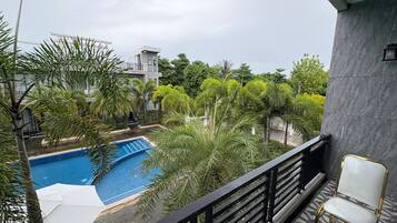 Uma varanda com vista para uma piscina, cercada por vegetação e um edifício moderno.