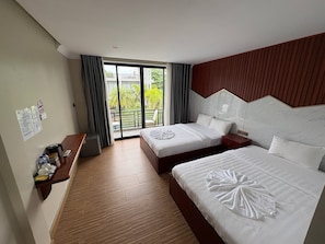 Quarto de hotel com duas camas, piso de madeira, varanda com vista e escrivaninha com cadeira.