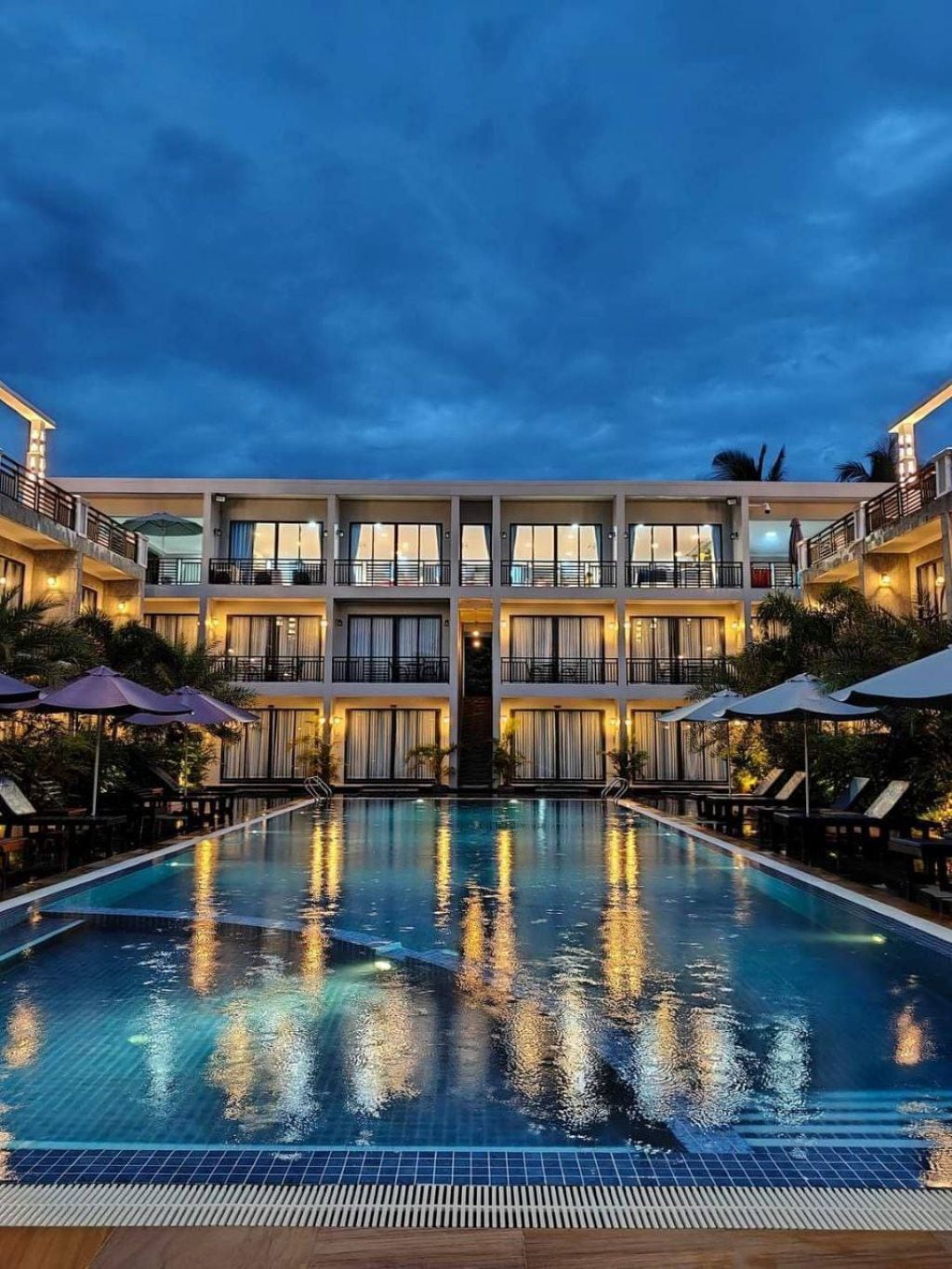 Um hotel de vários andares com piscina central, varandas e área de estar externa.