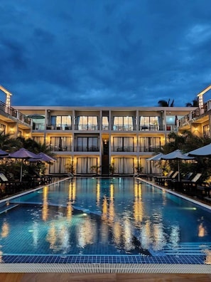 Um hotel de vários andares com piscina central, varandas e área de estar externa.